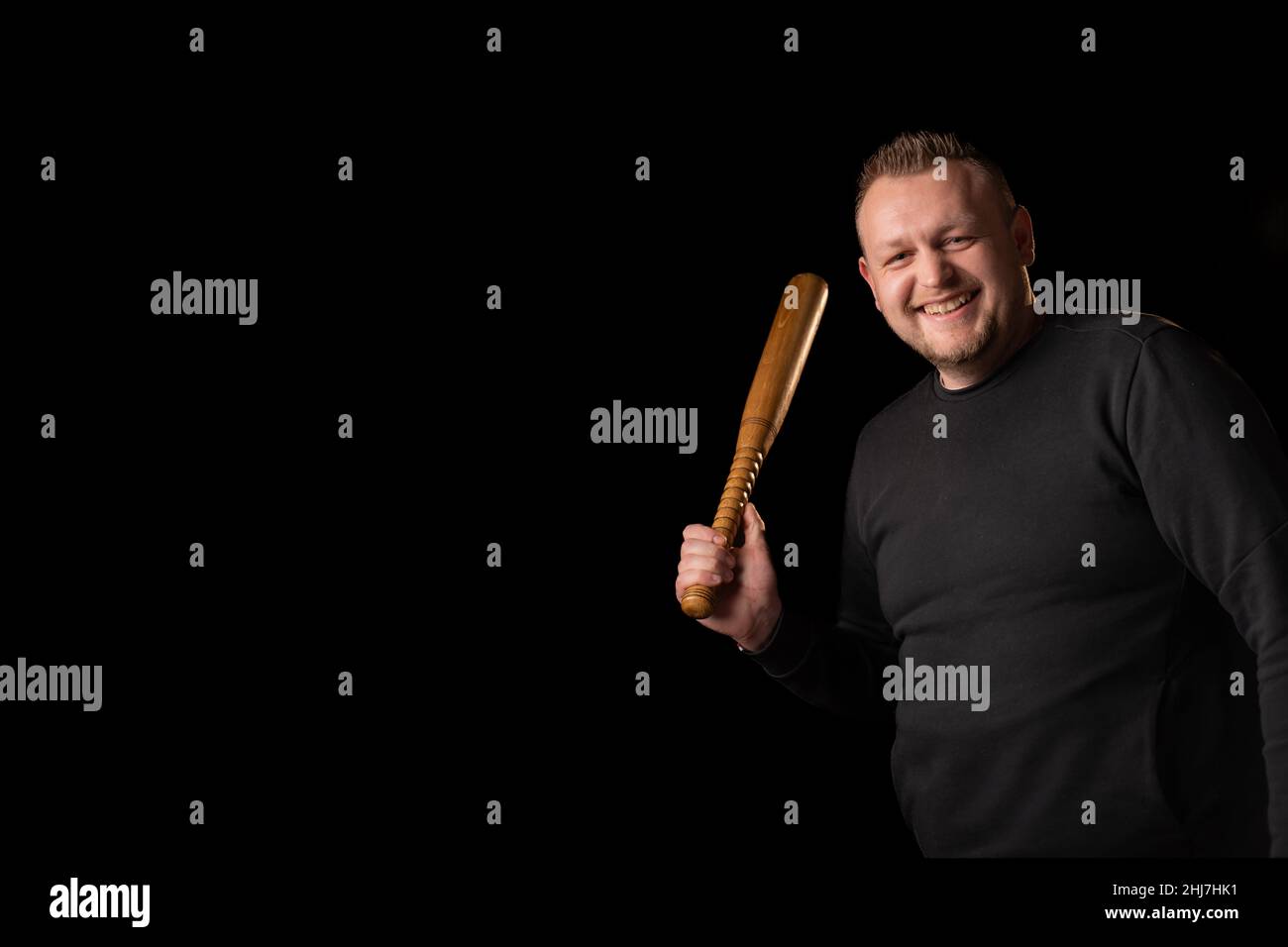 A young man holds a bat in his hand and smiles. Dark background. Place ...