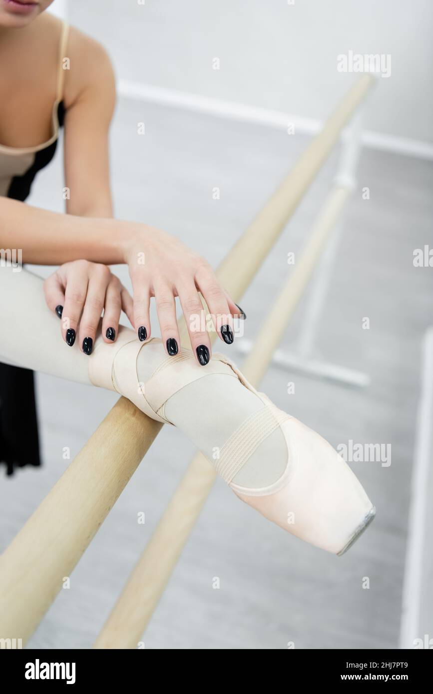cropped view of ballet dancer stretching leg at barre in dance studio ...