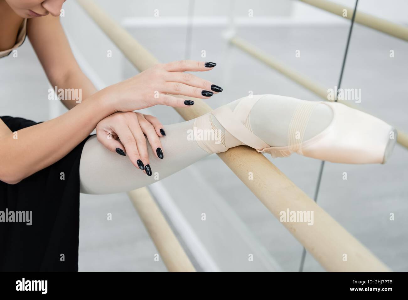 cropped view of ballerina stretching leg while training in dance studio ...