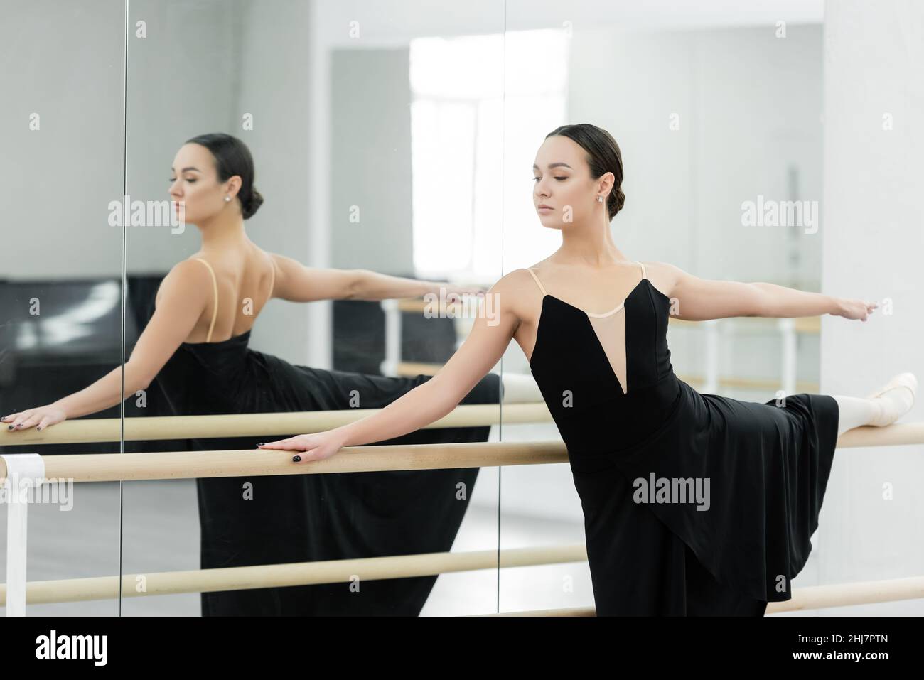 graceful woman in black dress training at barre in ballet studio Stock ...