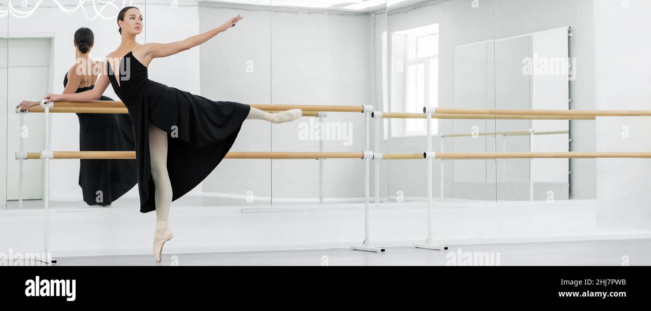 slim and graceful ballerina practicing ballet elements at barre in ...
