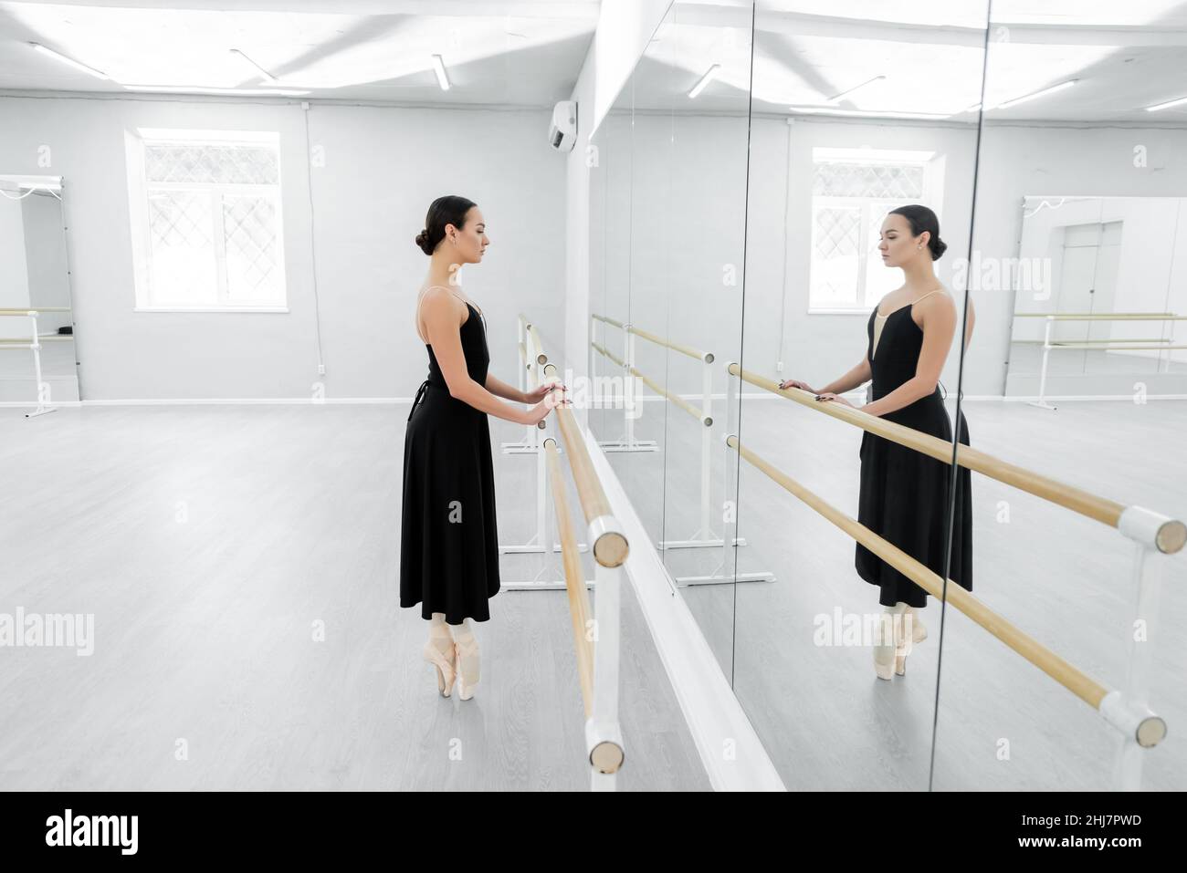 side view of ballet dancer in black dress standing on toes near barre ...