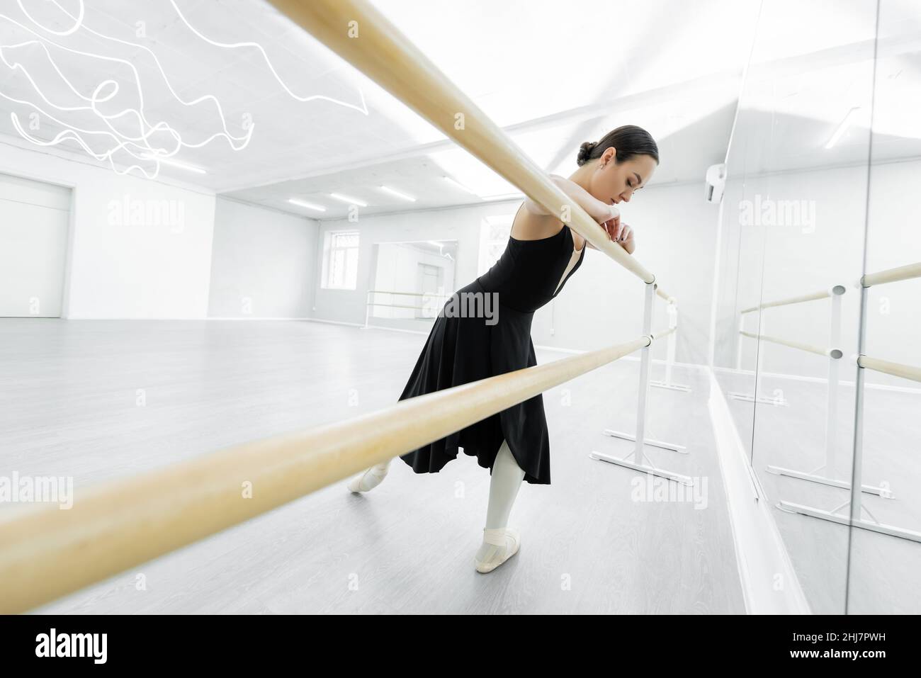 slim woman in black dress training at barre in ballet studio Stock ...