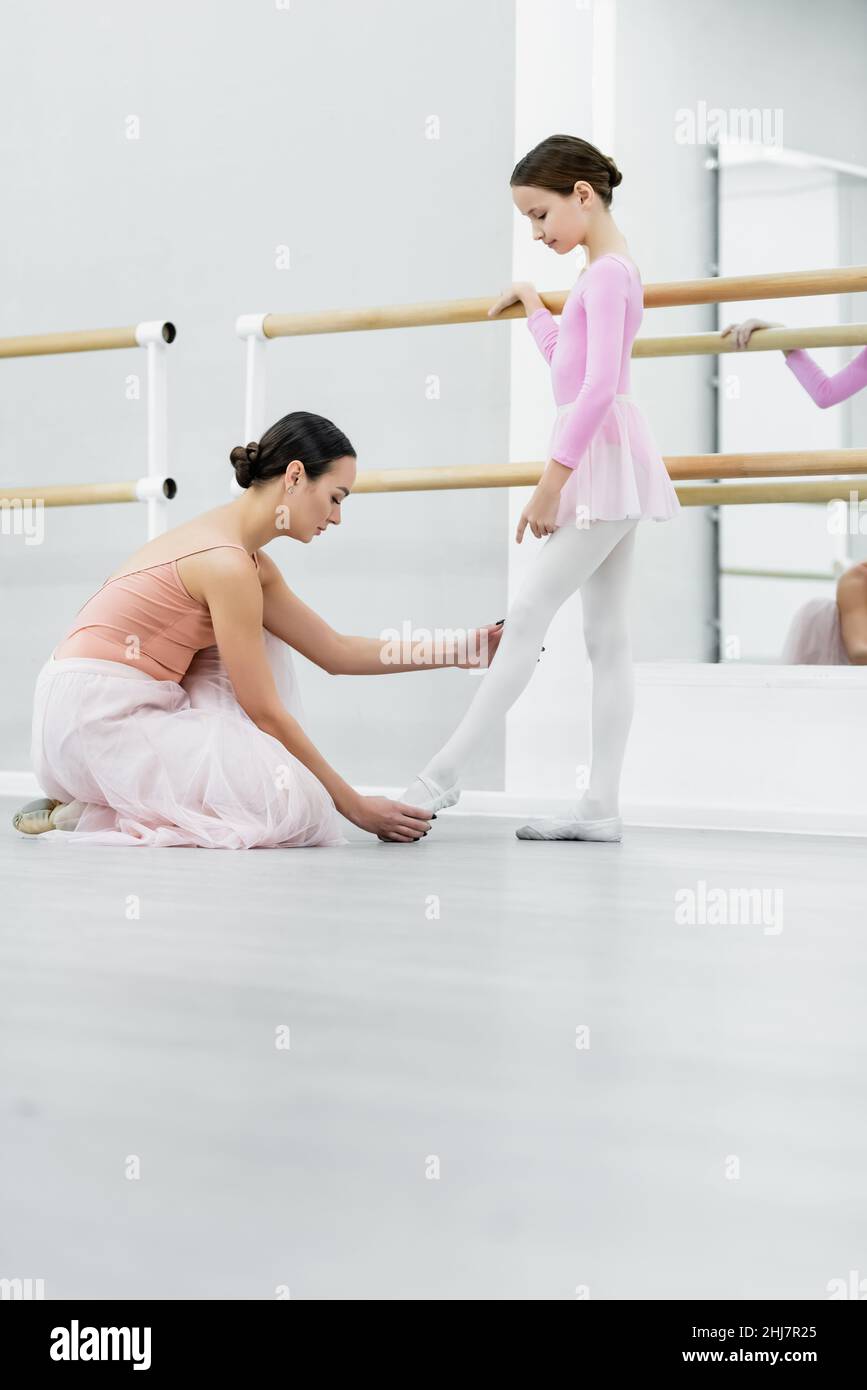 side view of dance teacher touching leg of girl training in ballet ...