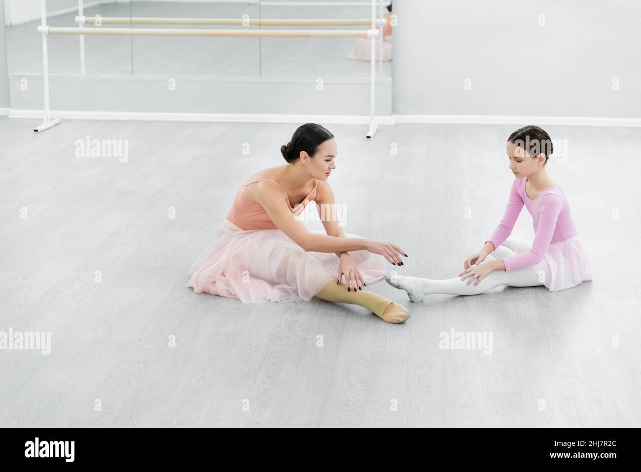 ballet teacher pointing with hand near girl stretching on floor in ...
