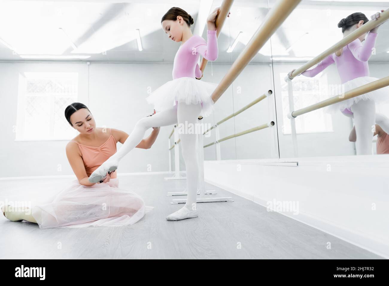 young ballet teacher touching leg of preteen girl during dance lesson ...