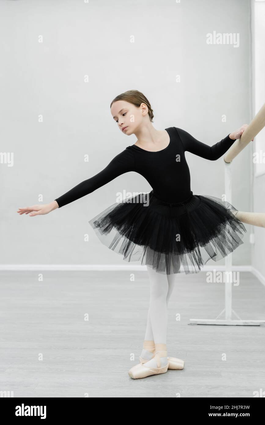full length view of graceful girl in black ballet costume training in ...