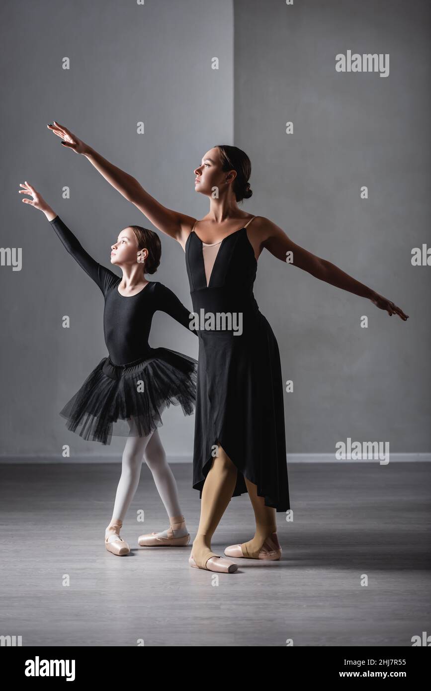 full length view of ballet teacher and girl in black tutu dancing ...