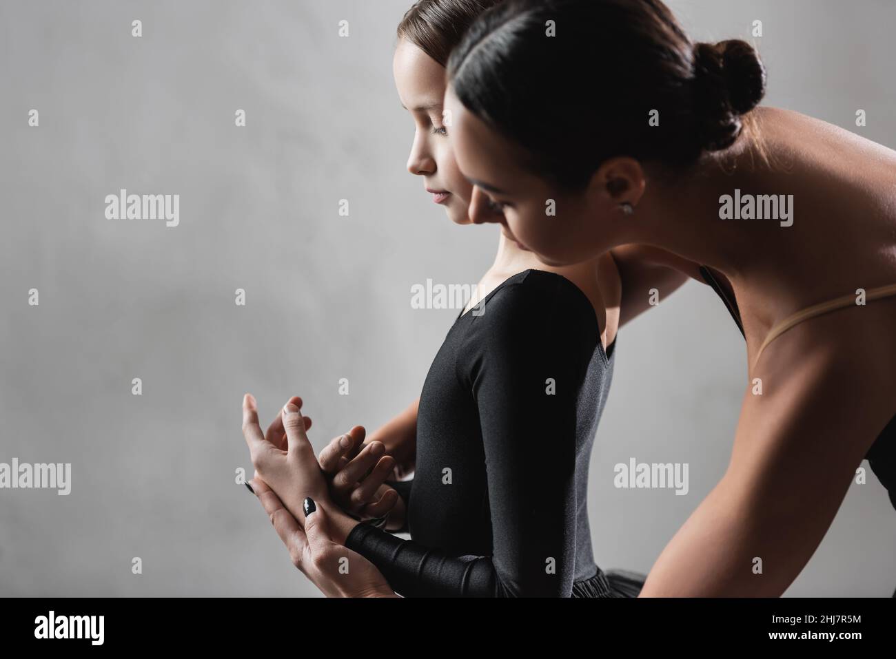 side view of ballet master teaching girl to dance on grey background ...