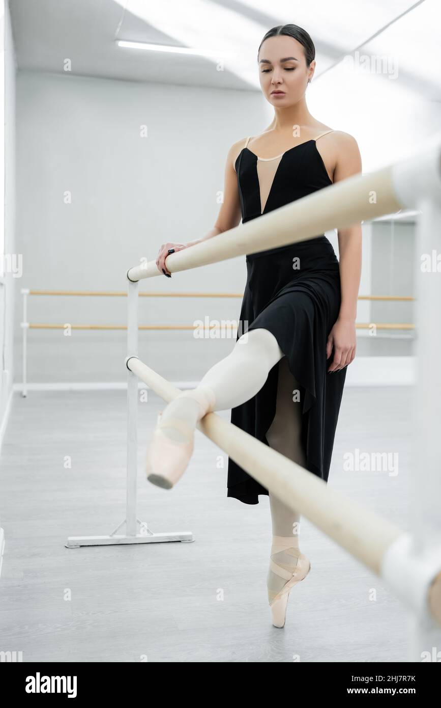 ballerina in black dress stretching at barre in dancing hall Stock ...