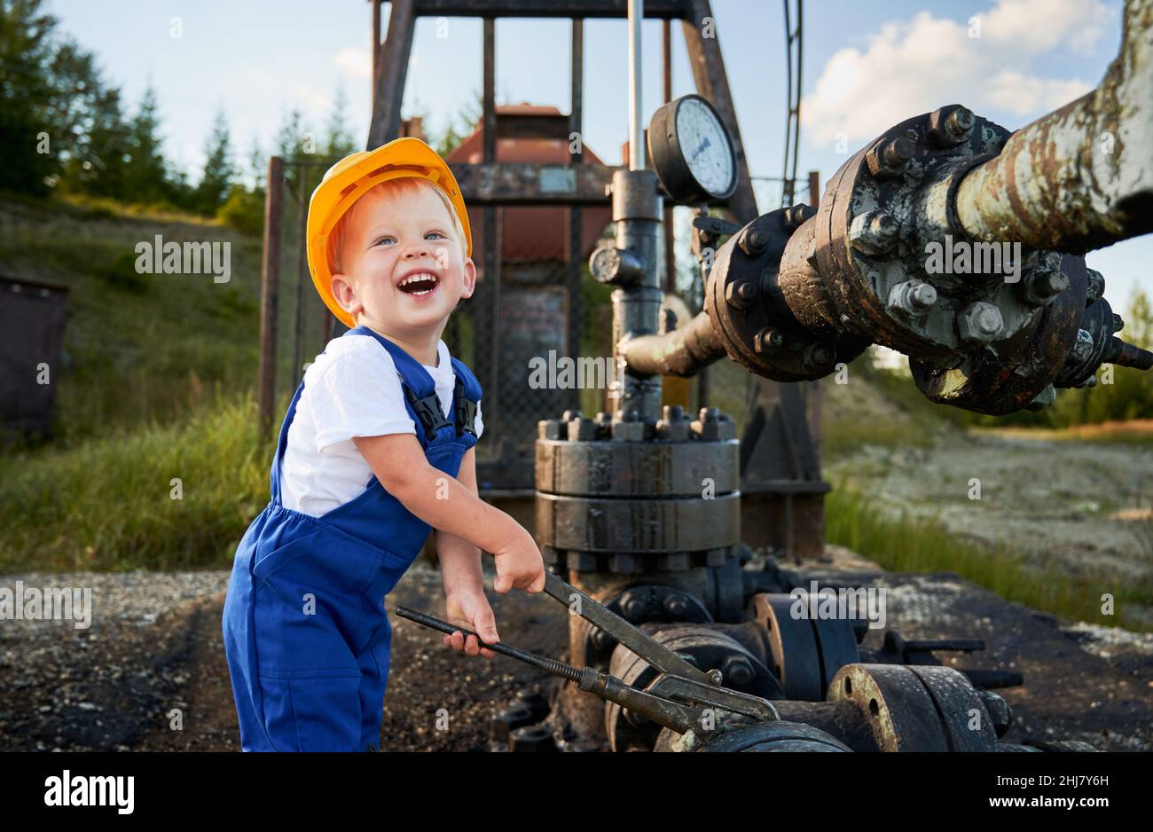Happy male child playing in the mechanic, holding wrench near pipeline ...