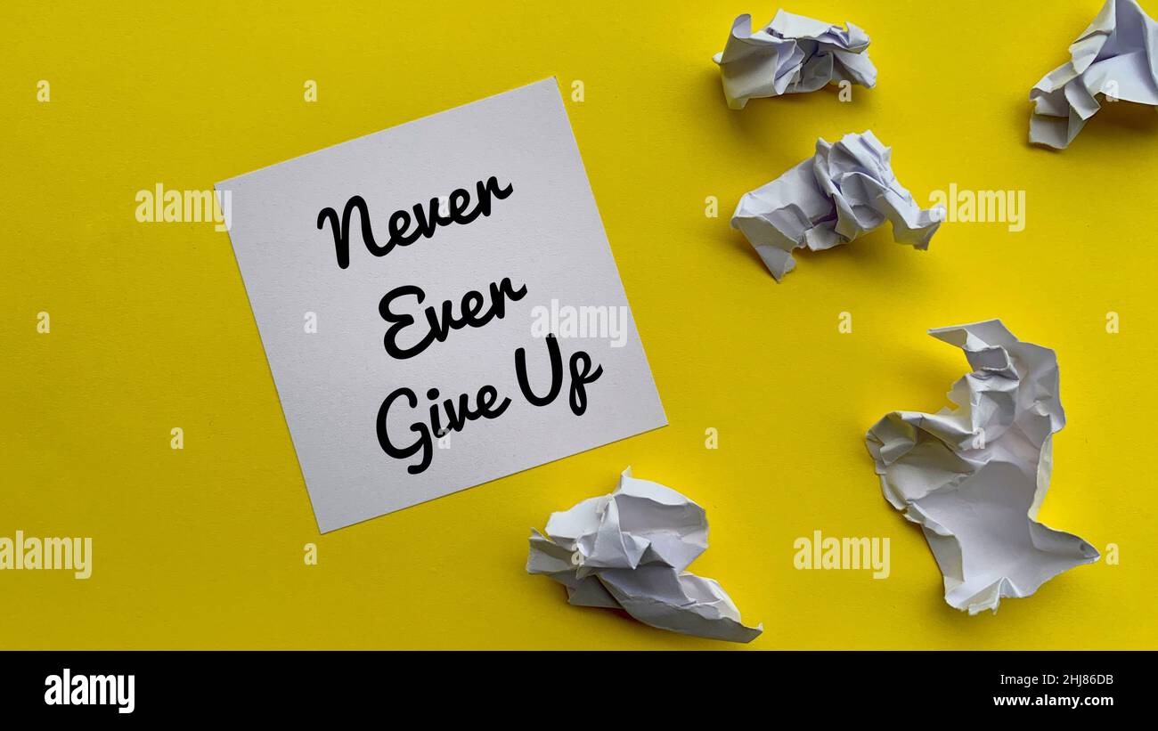 Top view of never ever give up text on notepad with trash papers and ...