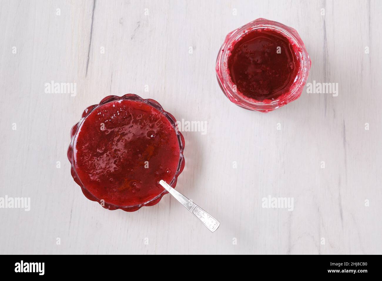 Top view of jar and saucer with cherry jam on white wooden background ...