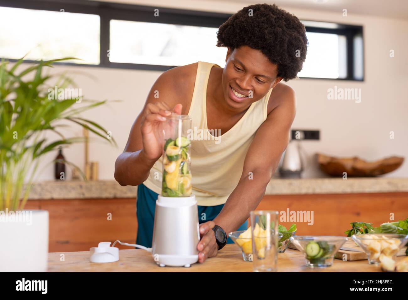 Smiling african american young man preparing smoothie in kitchen ...