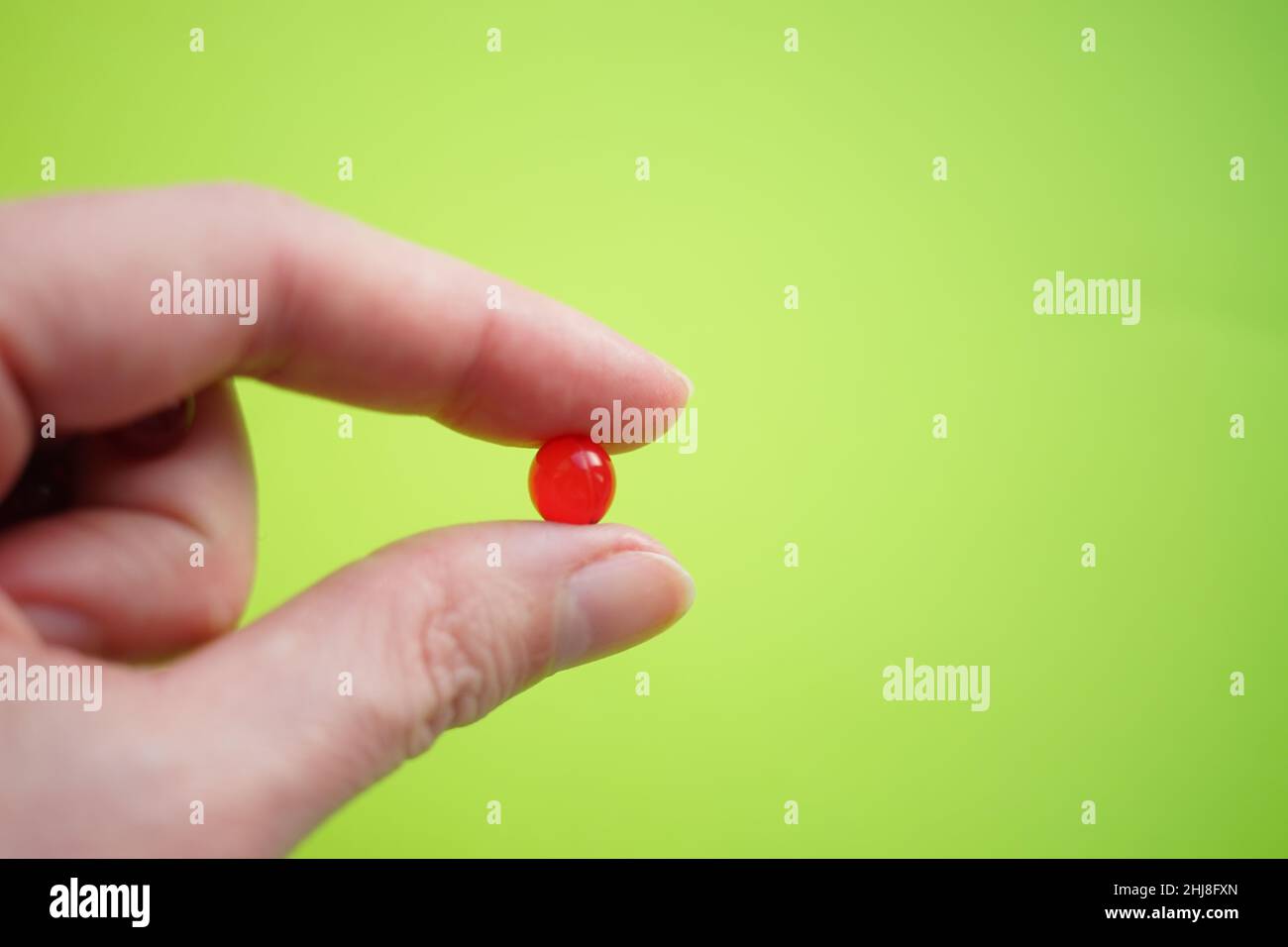 Round red vitamin in human fingers. Vivid green background Stock Photo ...
