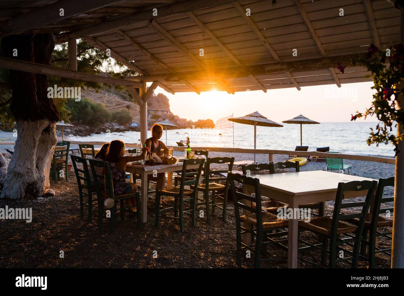 Family enjoying dinner in a restaurant on the beach at sunset. People ...