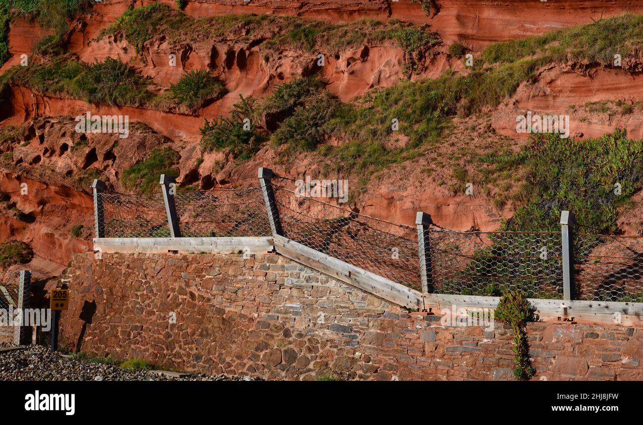 Red sandstone cliffs and rock-fall netting beside the coastal railway ...