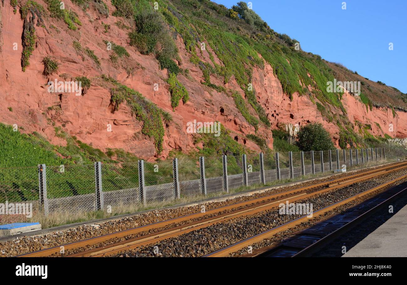 Red sandstone cliffs and rock-fall netting beside the coastal railway ...