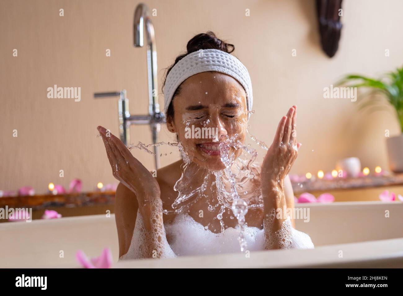 Smiling biracial young woman washing face in bathtub at spa. unaltered ...