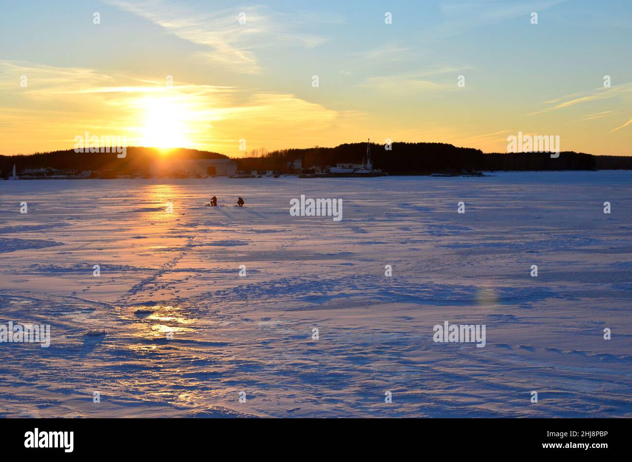 Two fishermen on a frozen lake catch fish in a hole of ice on the ...