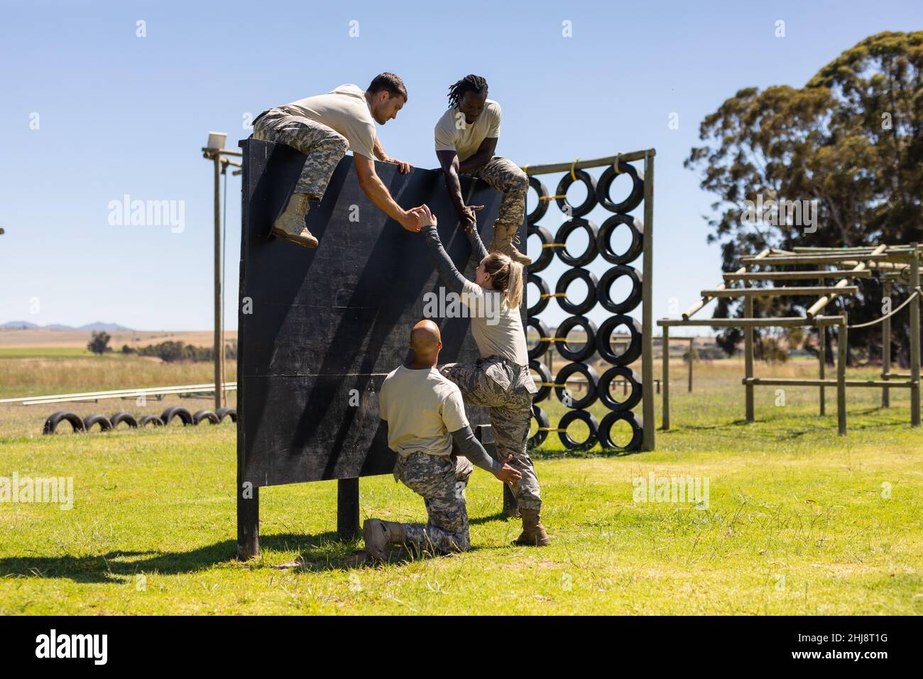 Two diverse male soldiers helping female caucasian soldier to climb ...