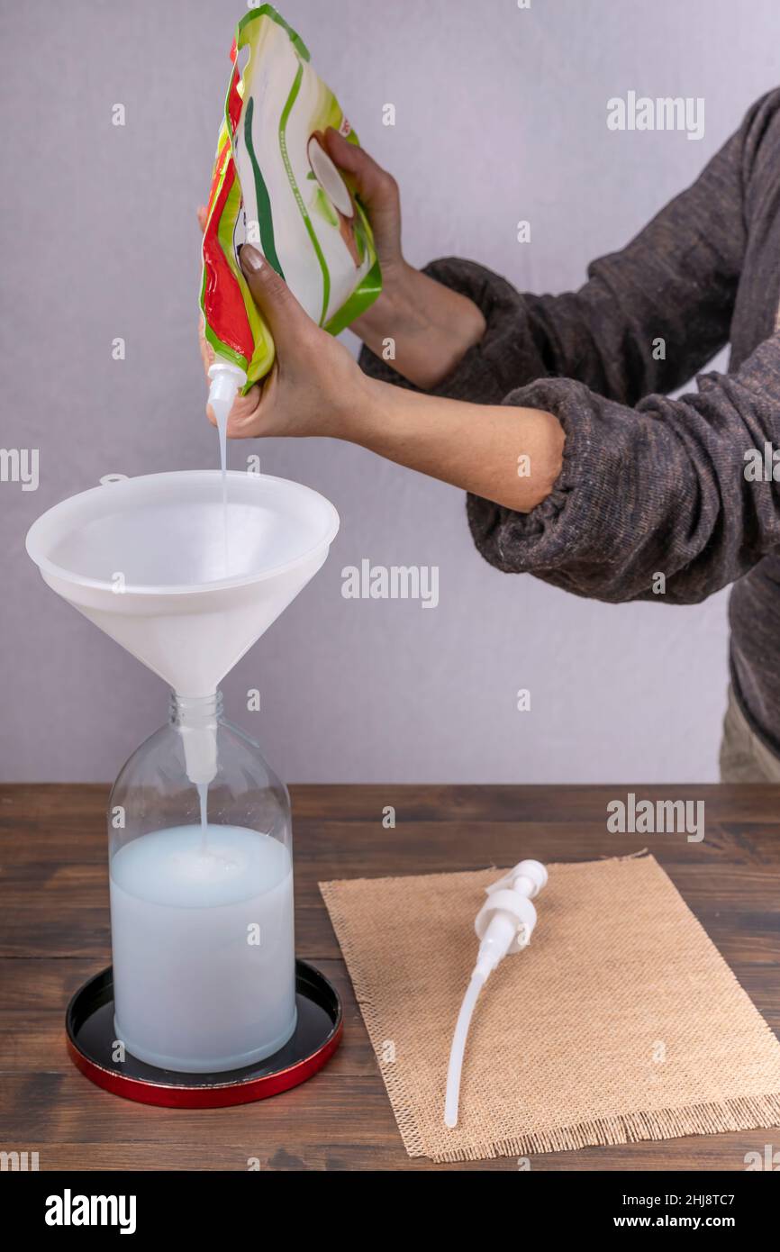 A woman fills a dispenser with liquid soap by pouring it from a refill ...