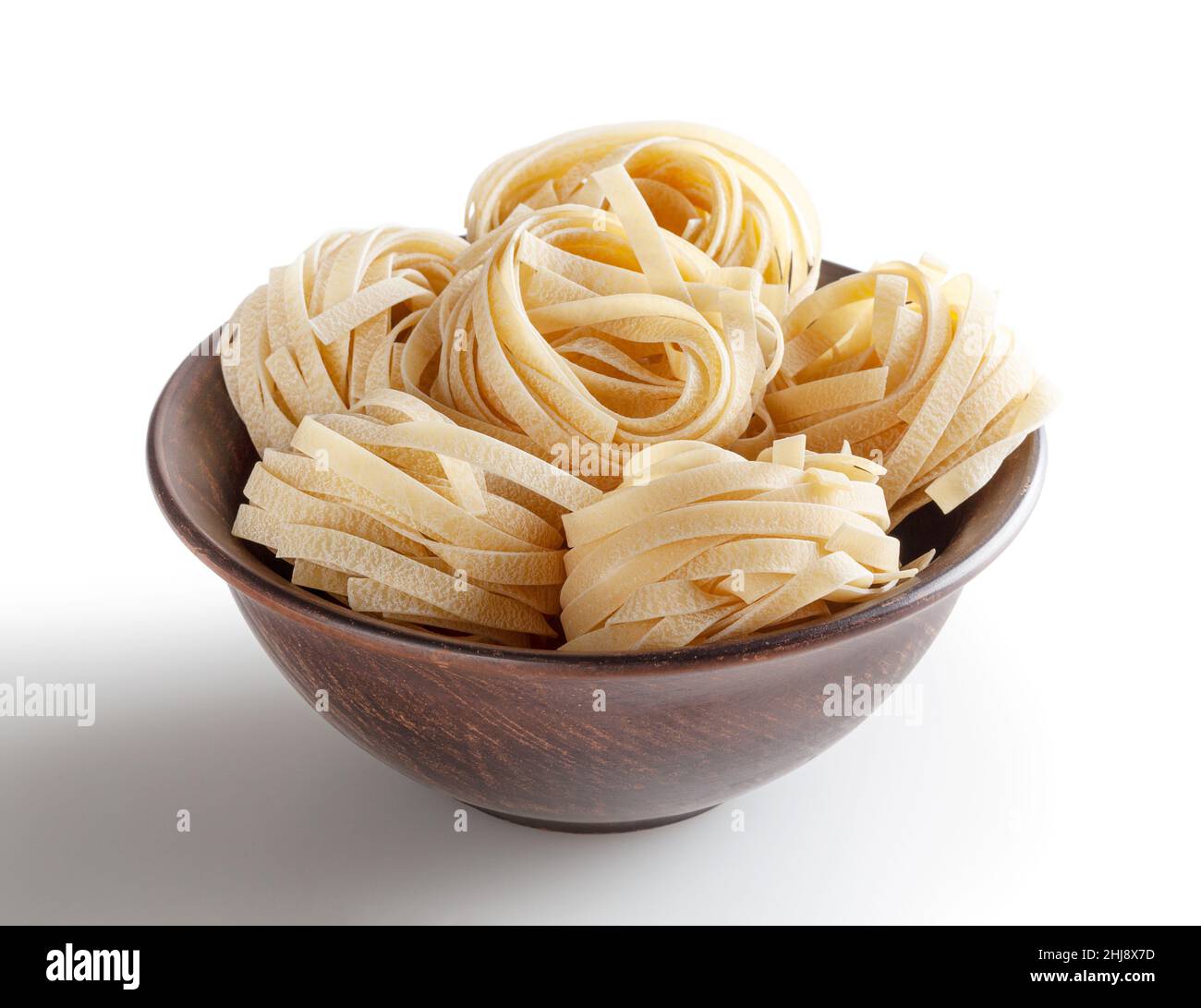Uncooked tagliatelle pasta in ceramic bowl isolated on white background ...