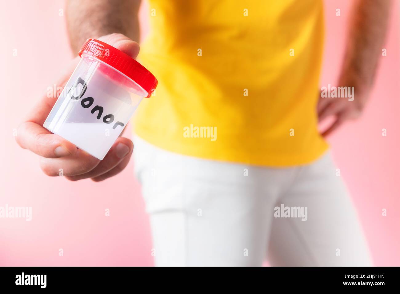 A man in white jeans holds a plastic jar with sperm sample with text ...