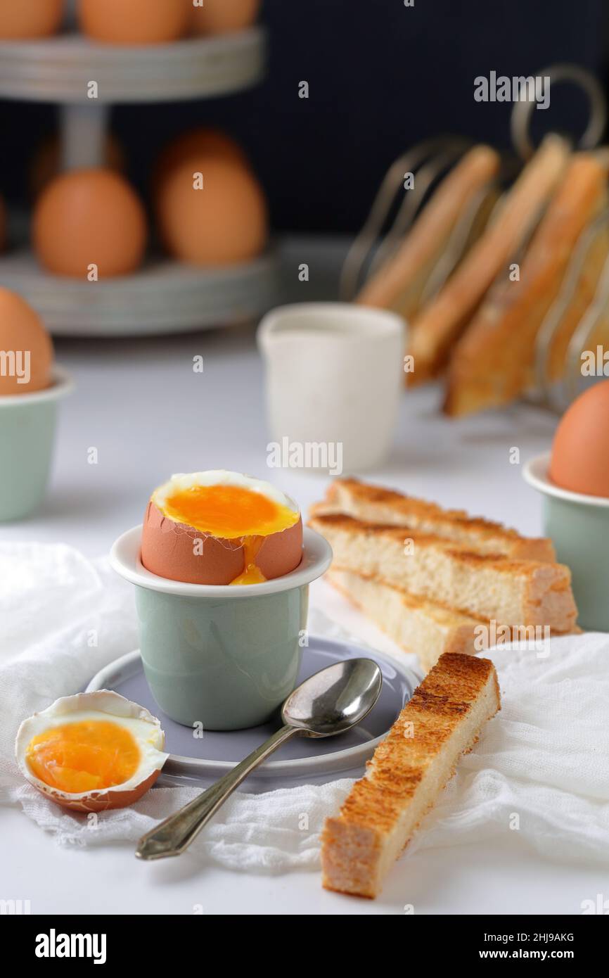A breakfast table with fresh free range soft boiled eggs with runny yolk in an egg cup with ...
