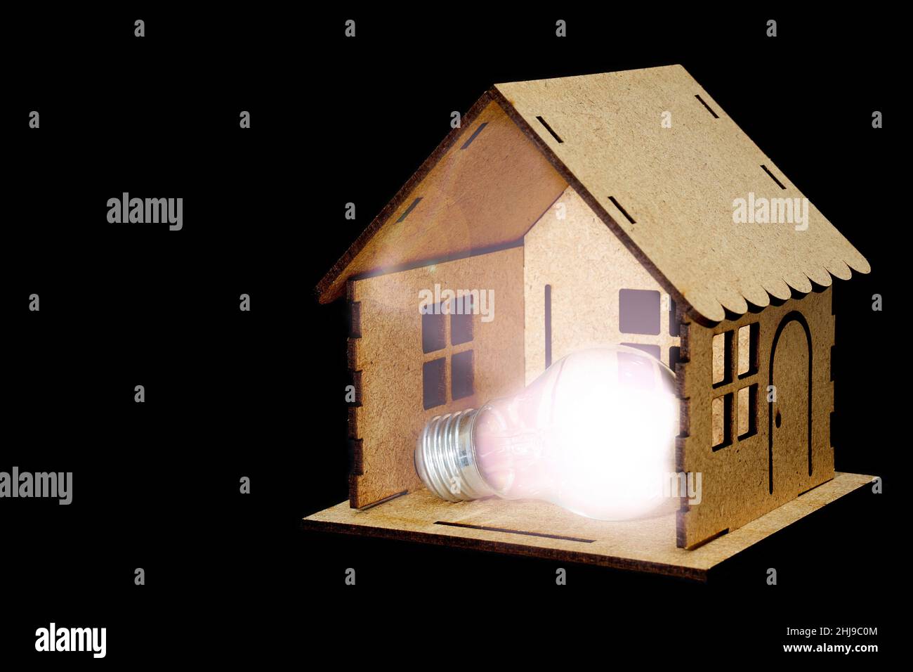 Glowing incandescent light bulb inside a miniature wooden house ...