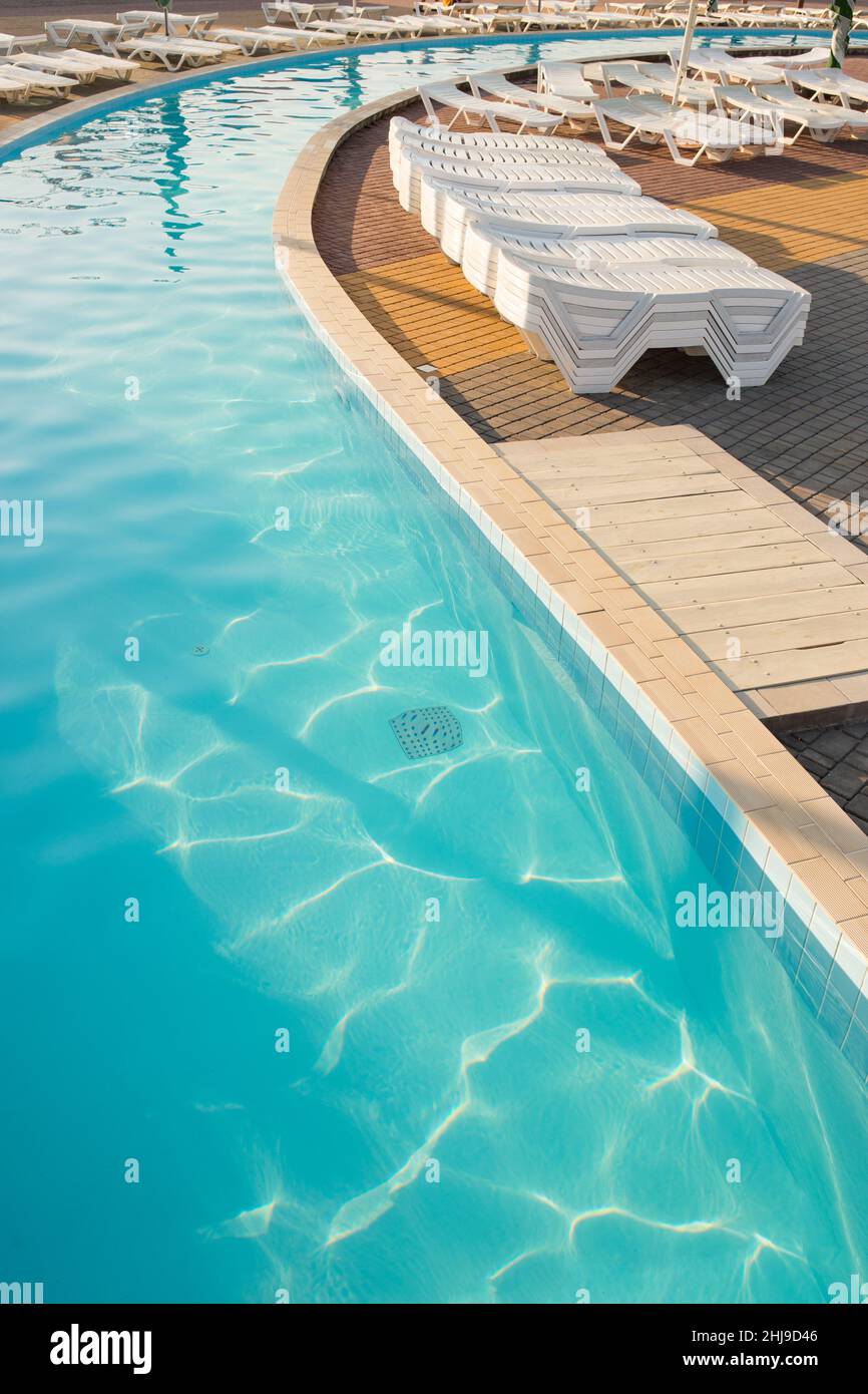 Swiming pool side at sunset time with sunbeds and blue clear water in ...