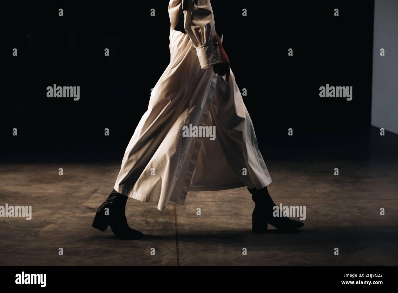 Cropped female figure dressed in a stylish long beige outfit walking ...