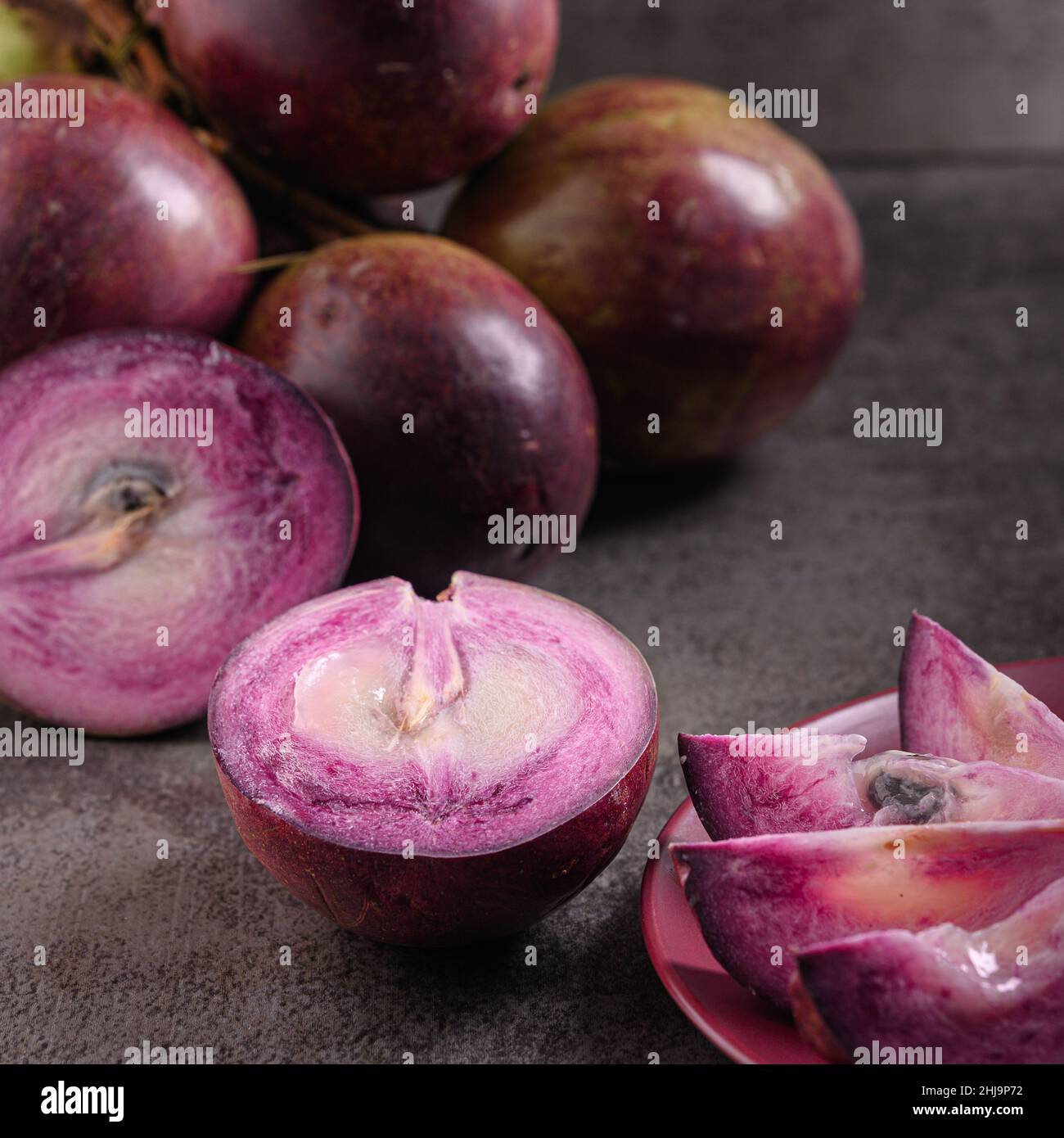 Photo shows several purple tropical fruits. One fruit is cut open and ...