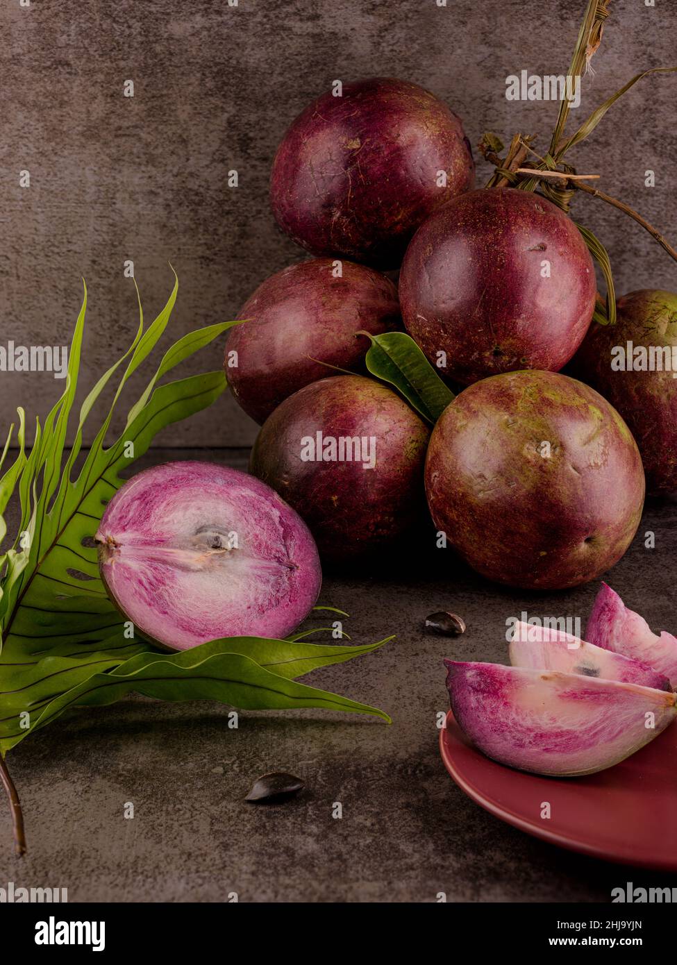 Photo shows several purple tropical fruits. One fruit is cut open and ...