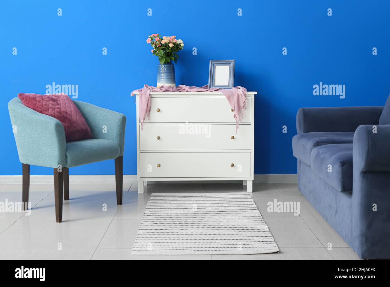 Beautiful roses in vase with frame on chest of drawers, armchair and ...