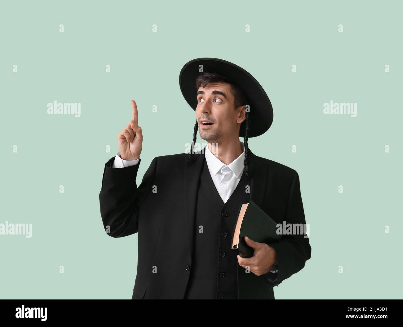 Hasidic Jewish man with Torah pointing at something on color background ...