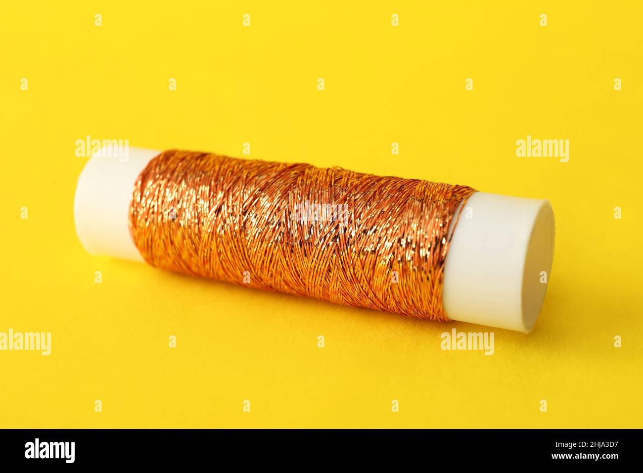 Golden sewing thread spool on color background Stock Photo - Alamy