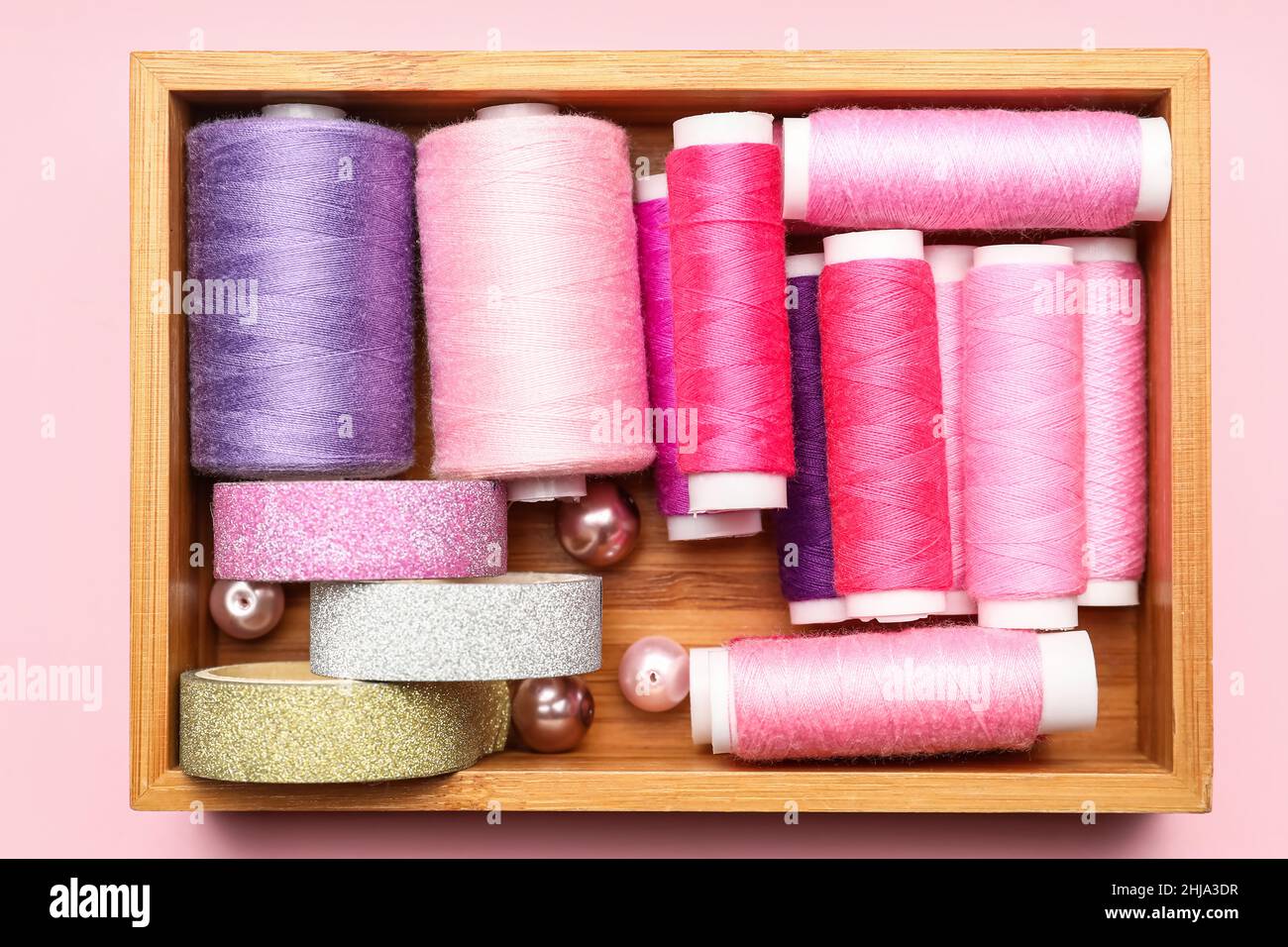 Wooden box with different sewing thread spools and tapes on color ...