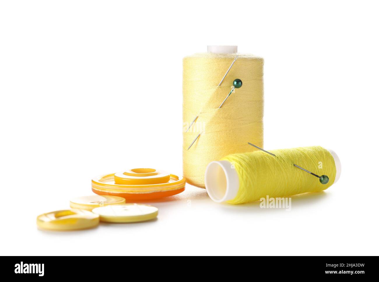Yellow sewing thread spools with pins and buttons on white background ...