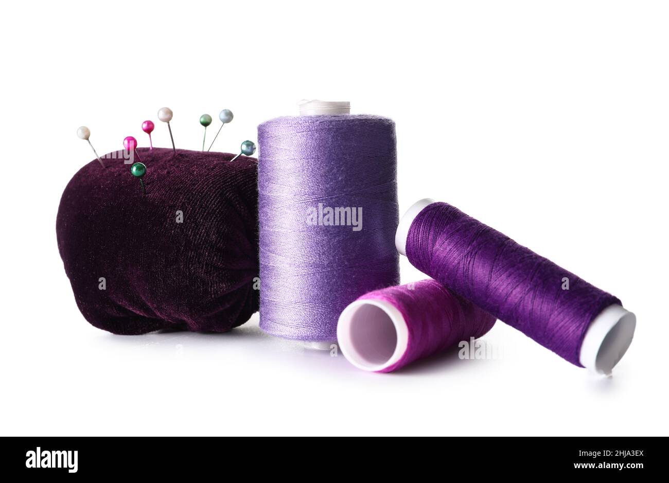 Purple sewing thread spools and pincushion with pins on white ...