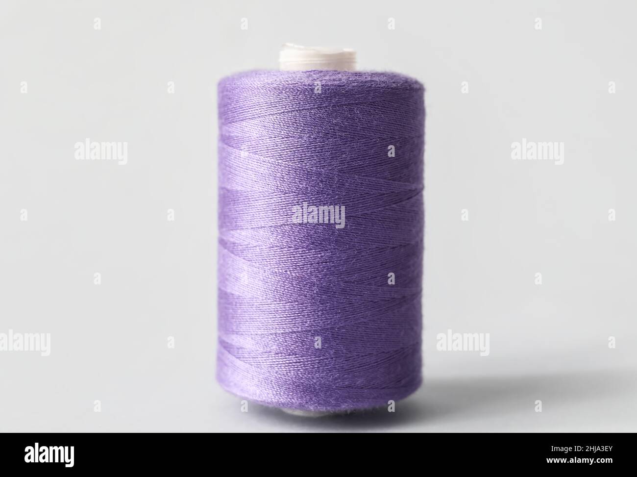 Purple sewing thread spool on light background Stock Photo - Alamy