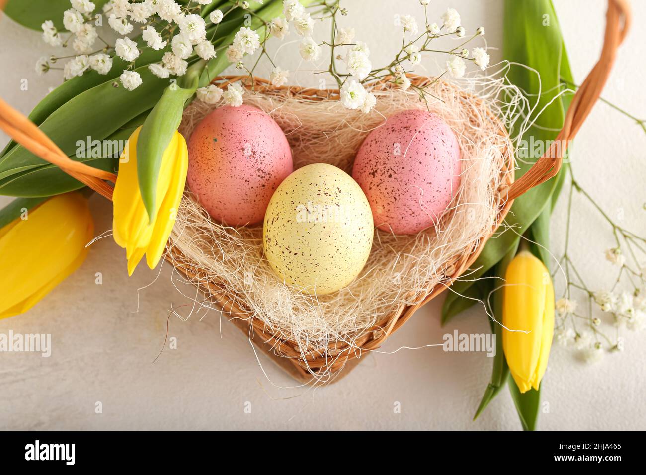 Basket with beautiful Easter eggs and spring flowers on light ...