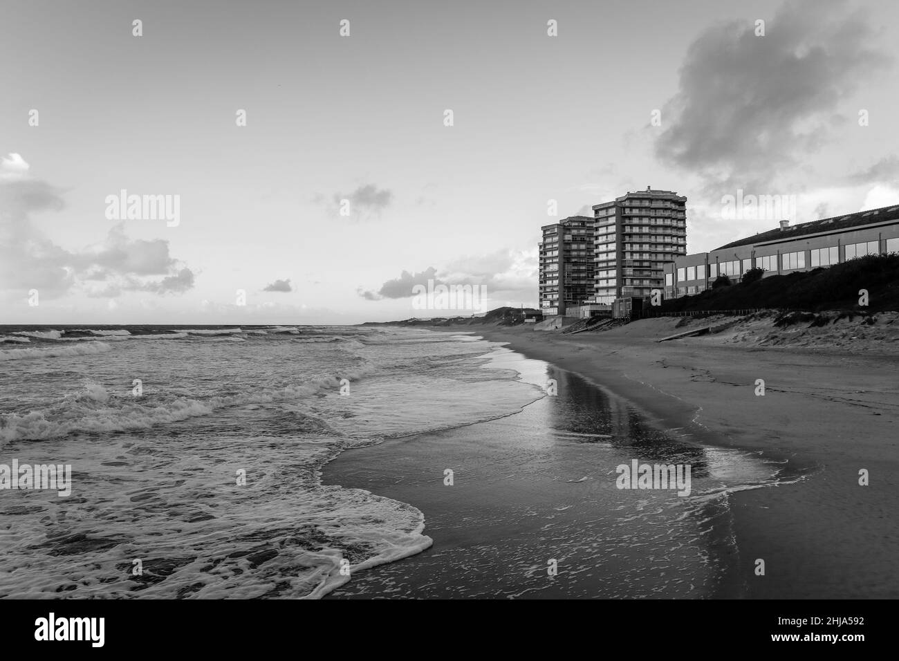 Grayscale shot of buildings on the beach by the sea under a cloudy sky ...