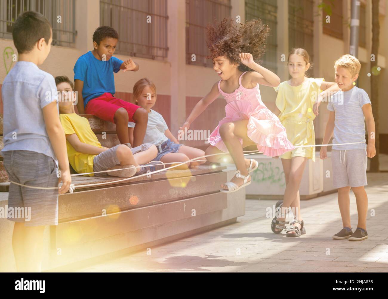Energetic kids playing and skipping on elastic jumping rope in yard ...