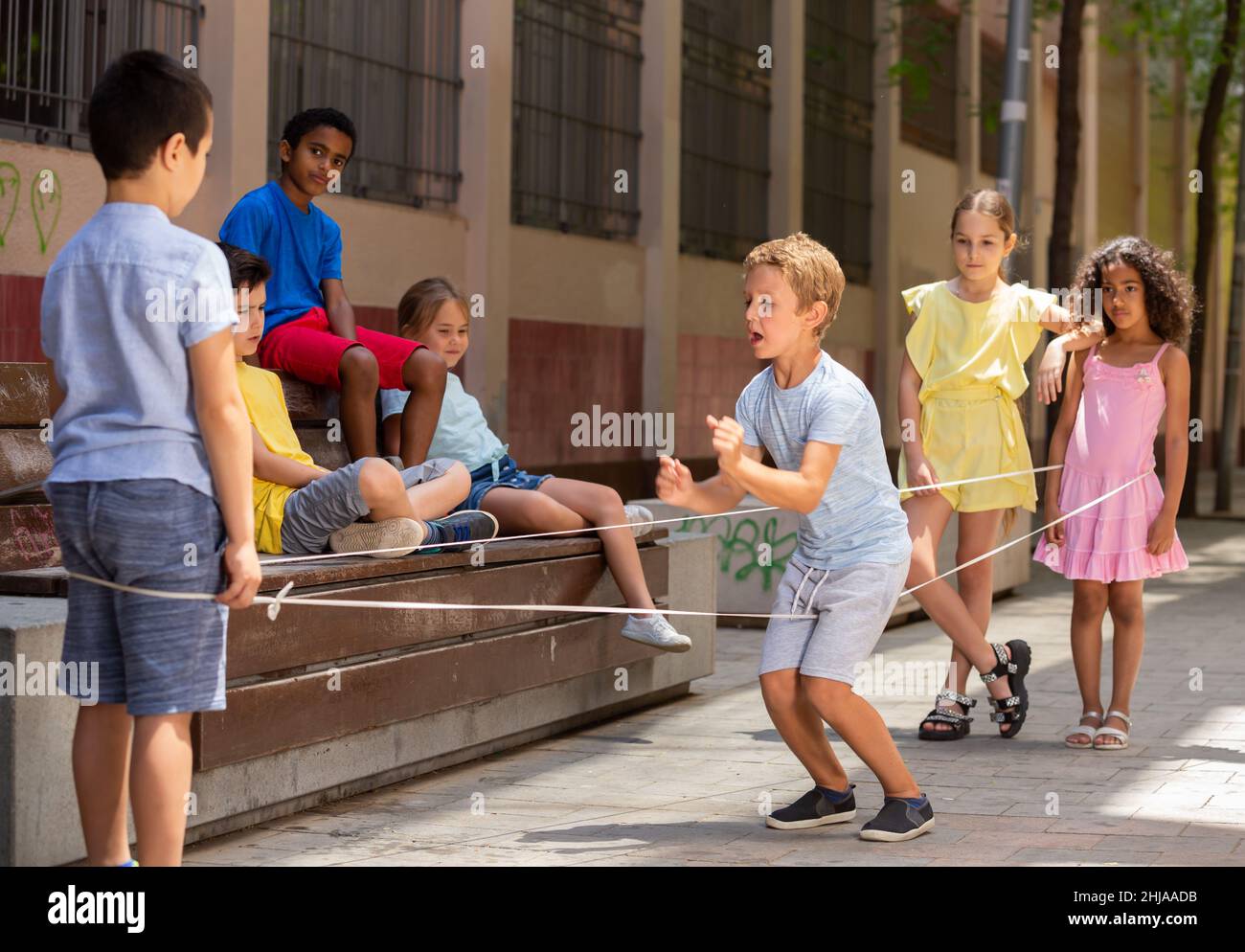 Energetic kids playing and skipping on elastic jumping rope in yard ...
