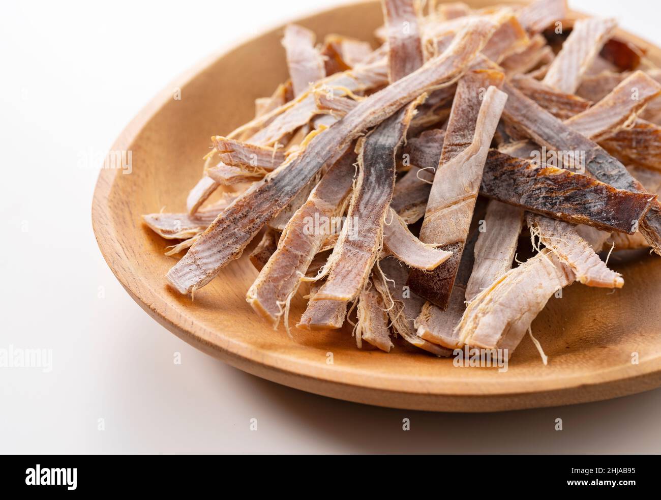 Dried squid served on a wooden plate set against a white background ...