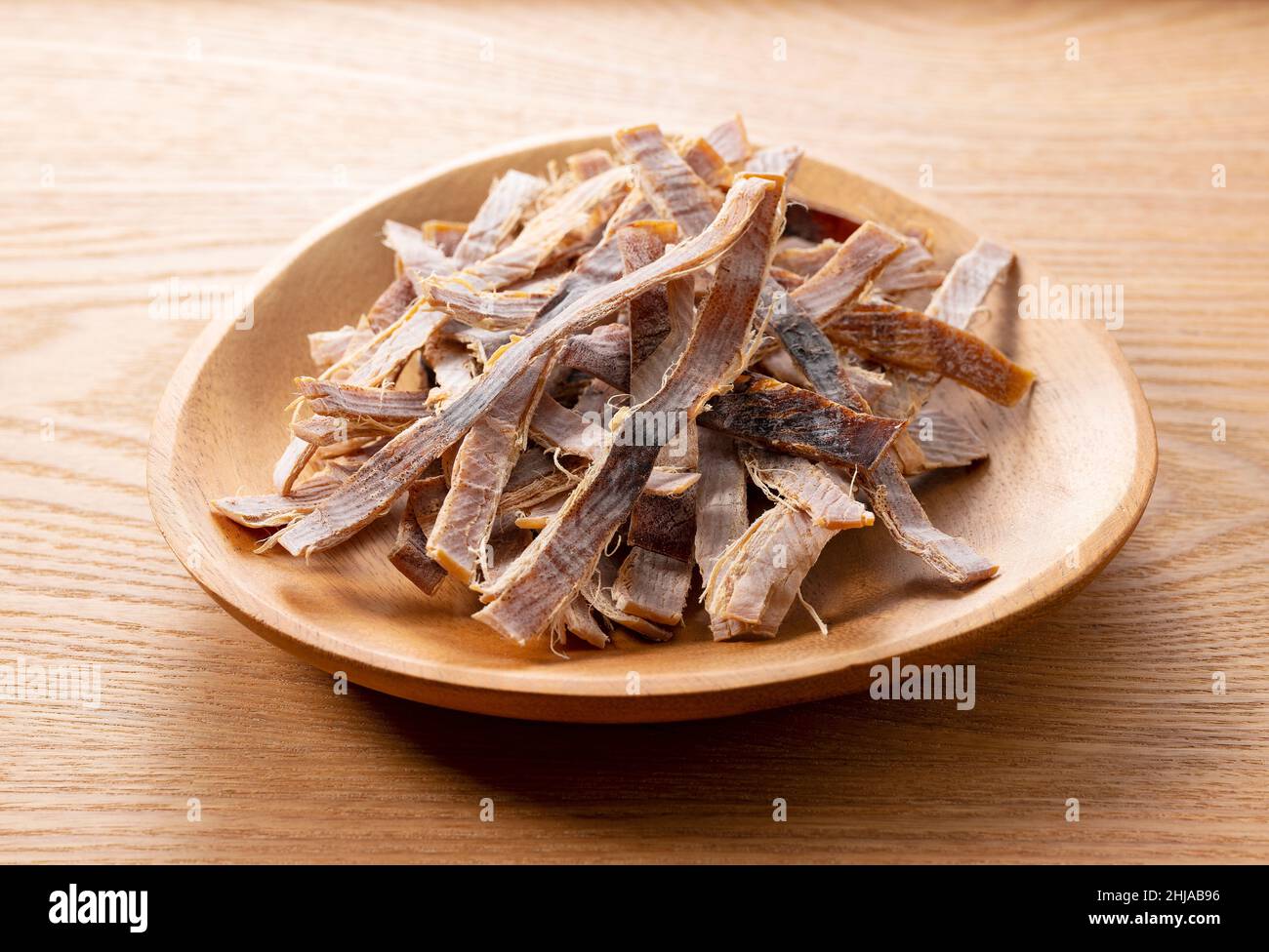 Dried squid served on a wooden plate set against a wooden background ...