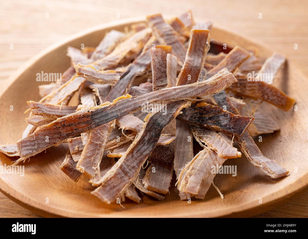 Dried squid served on a wooden plate set against a wooden background ...