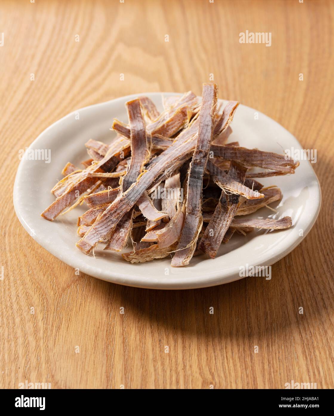Dried squid on a plate set against a wooden background. Surume is a ...