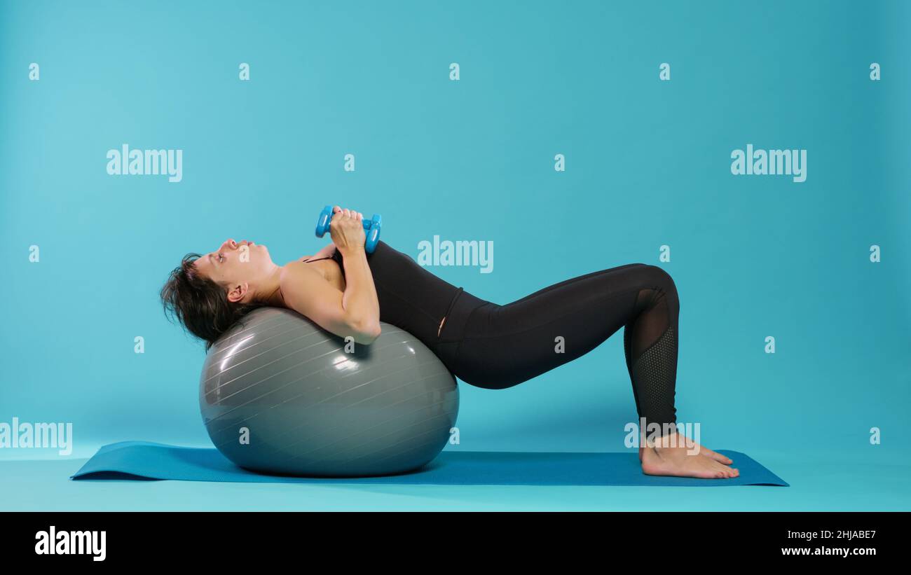 Active woman lifting dumbbells on fitness toning ball, doing physical ...